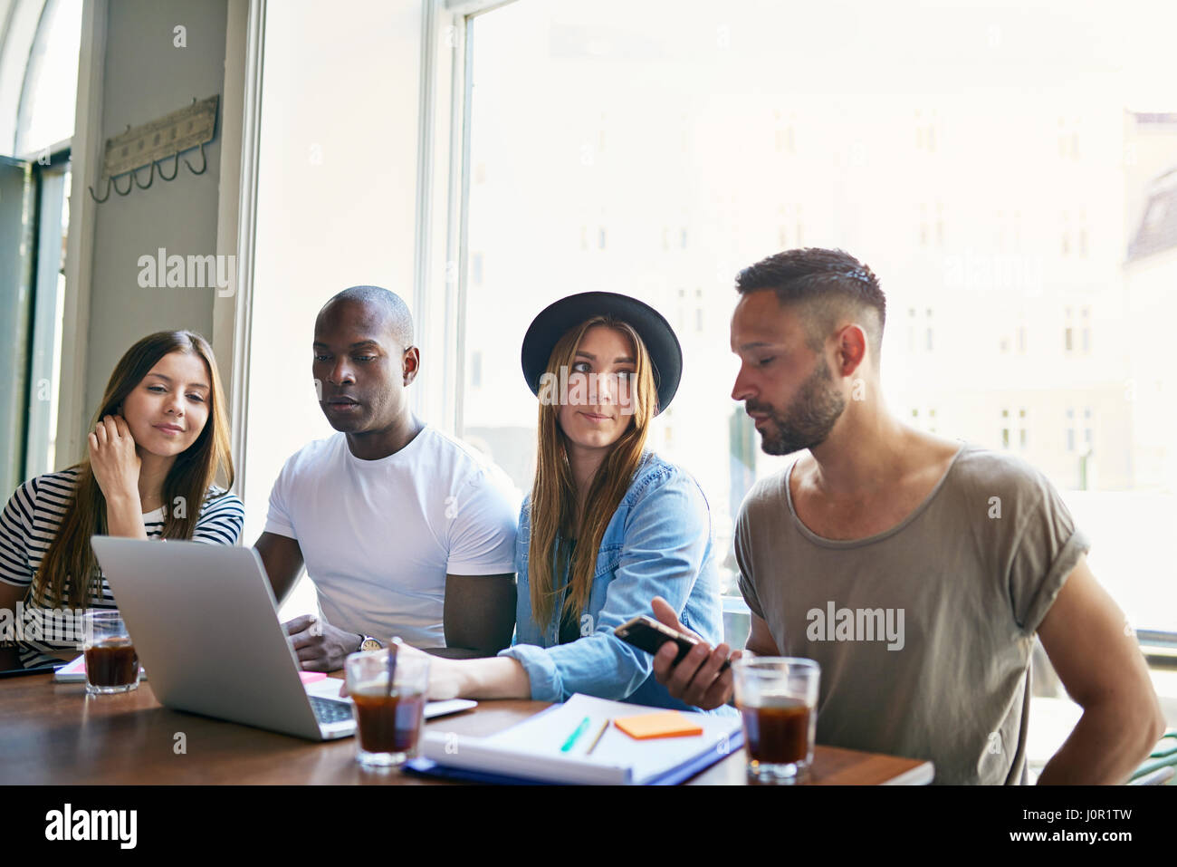 Group of four young co-workers sitting at table with laptop and having ...