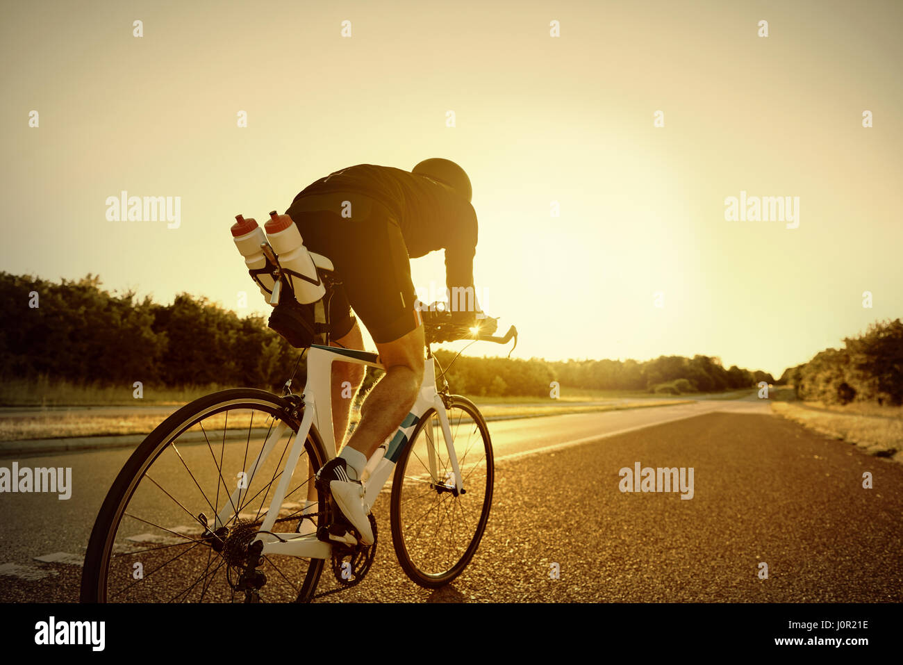 Back view of a cyclist riding a professional bike on empty highway ...