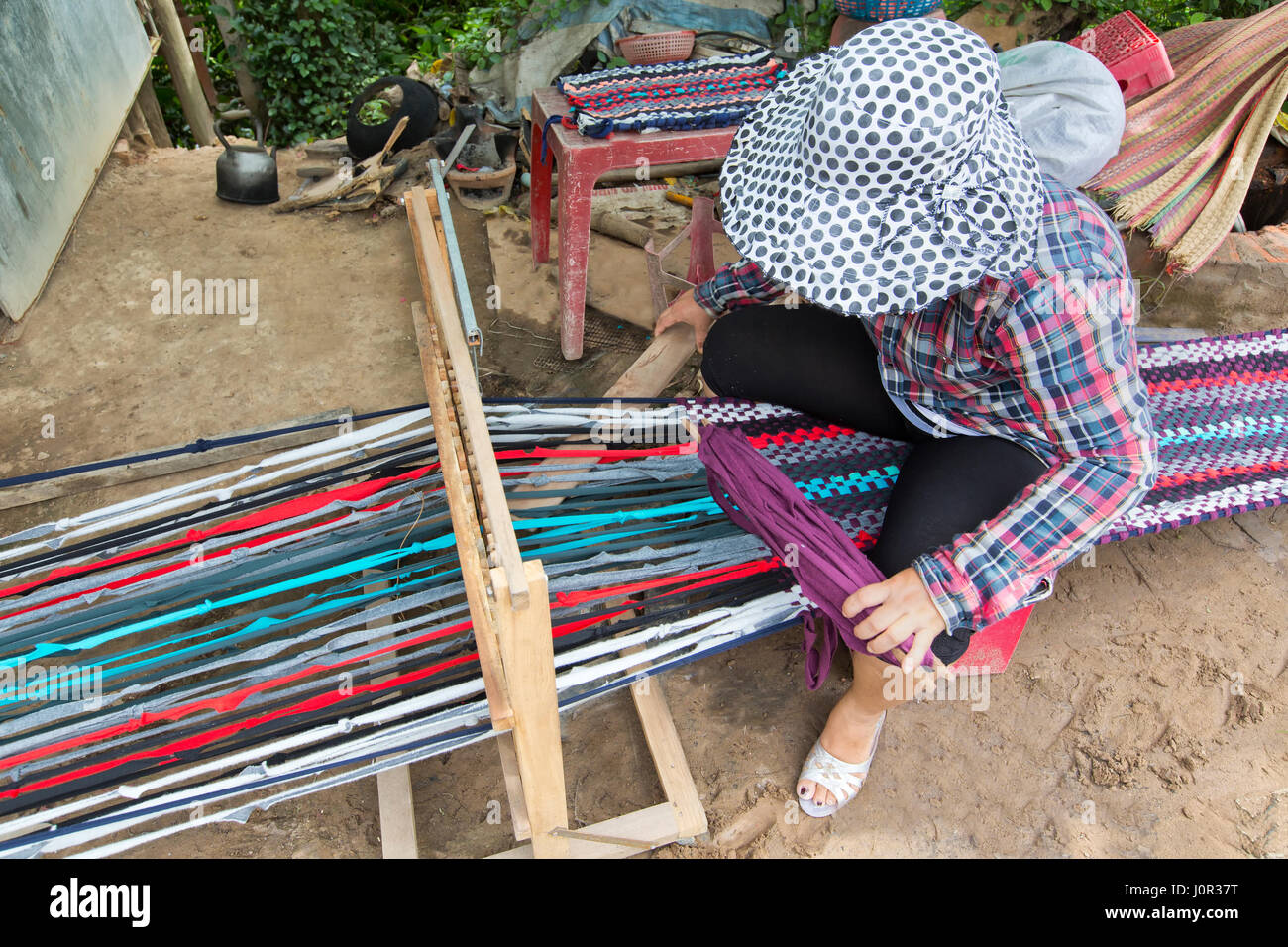 Woman working at loom, holding spindle, weaving extended rug (18 meters ...