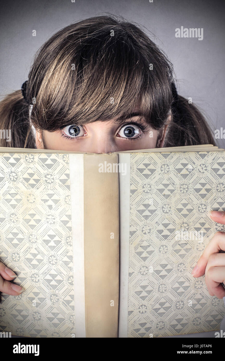 Girl hiding behind book Stock Photo - Alamy