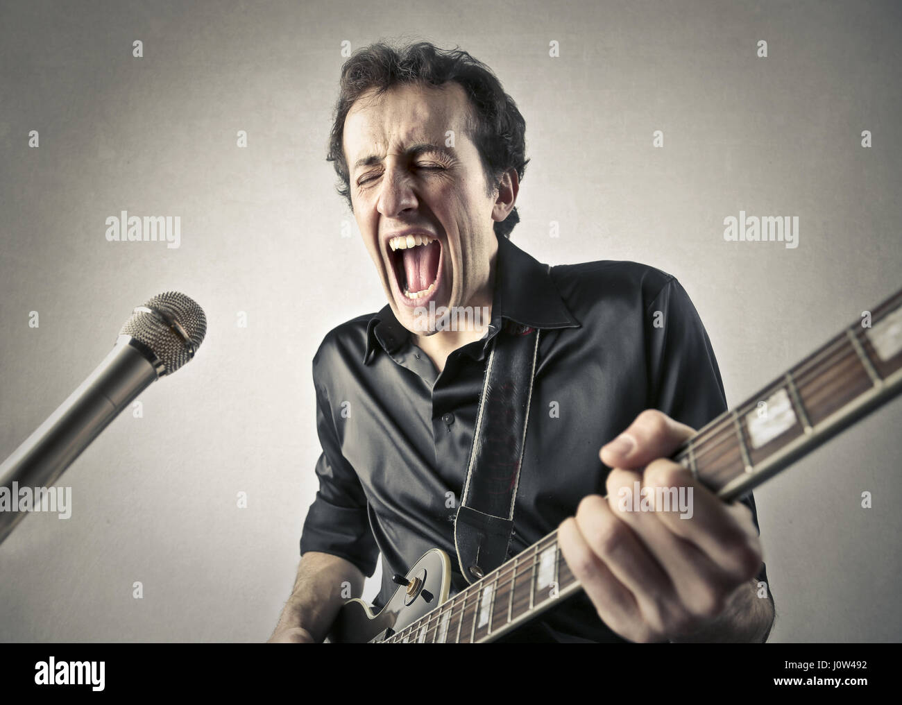 Man singing in microphone while playing on guitar Stock Photo - Alamy