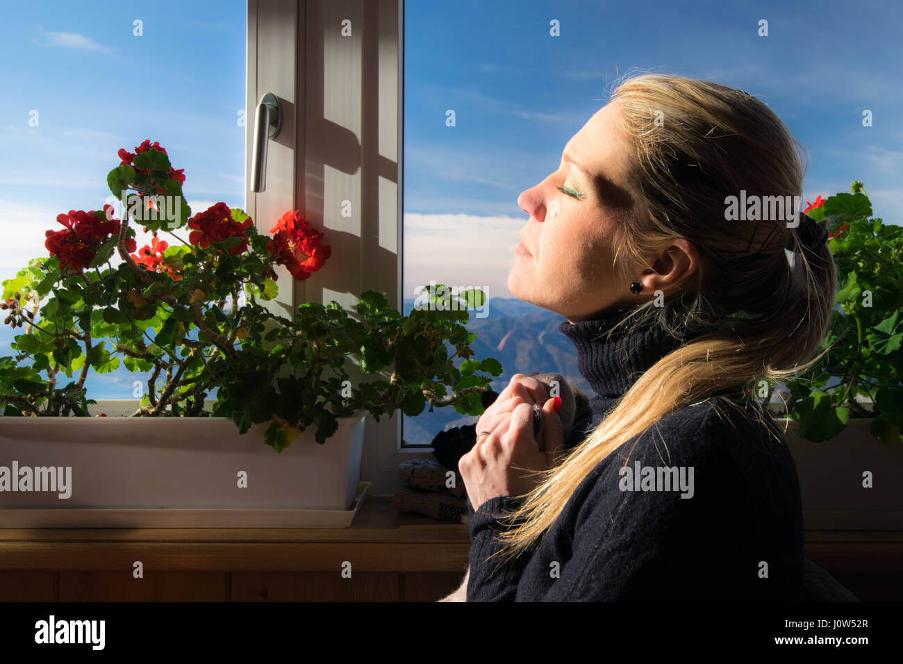 Woman closes her eyes and warms up at the rays of the sun filtering ...