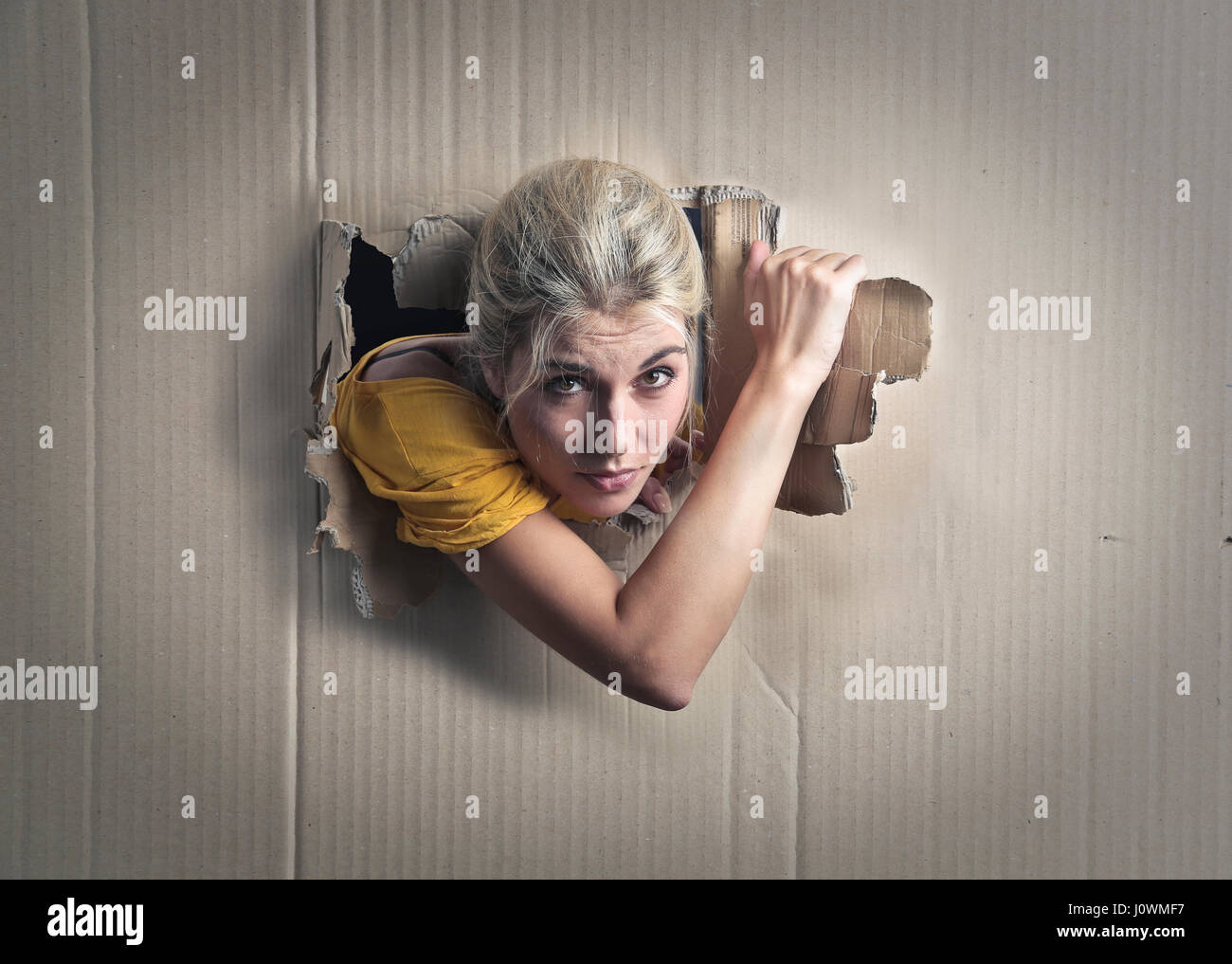 Blond woman breaking through paper wall Stock Photo - Alamy