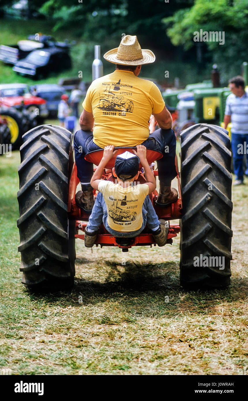 Young boy hitching a ride on to the back of an antique tractor riding ...