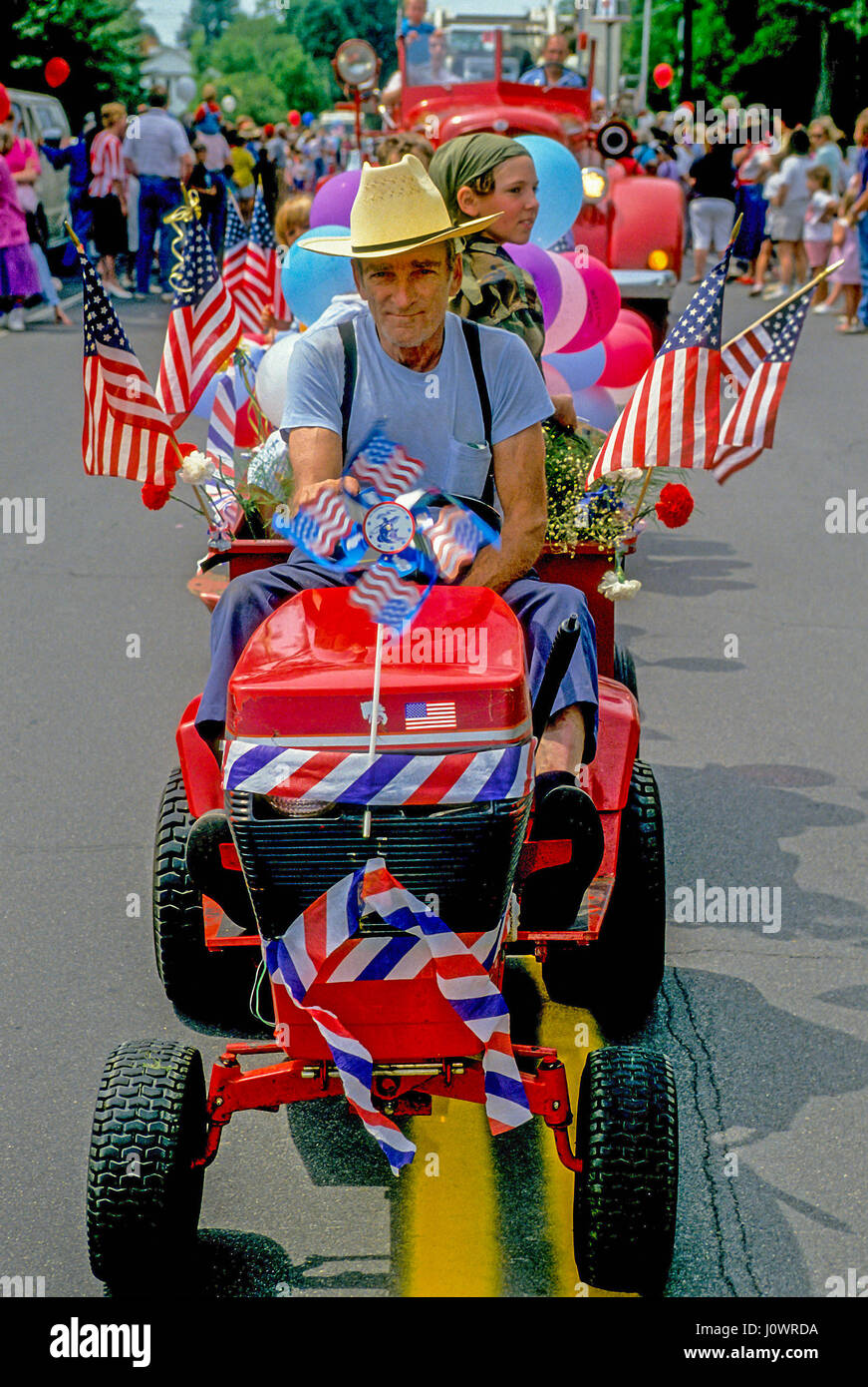Man in a straw hat drives a mini tractor decorated with American flags ...