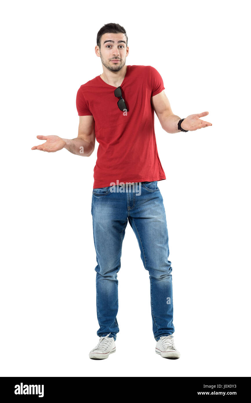 Puzzled young casual man in red t-shirt shrugging shoulders looking at ...