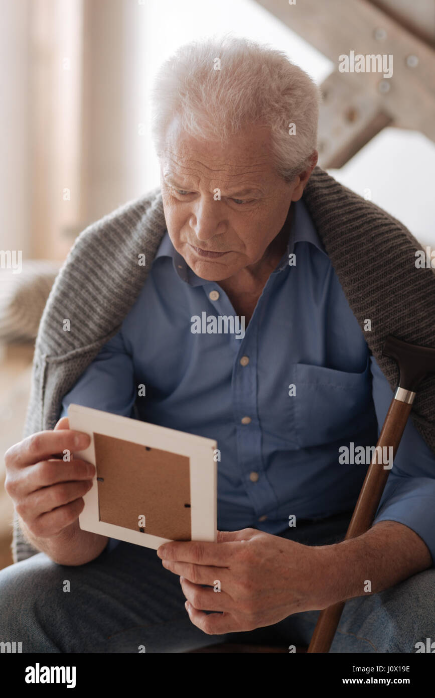 Sad feelings. Unhappy grey haired man holding a photo of his wife and ...