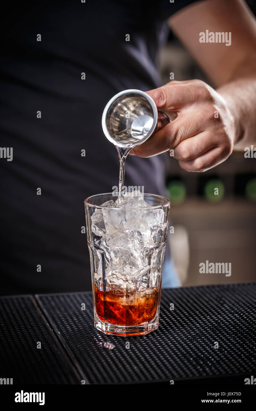 Barman is pouring alcohol from a jigger into a glass over ice ...