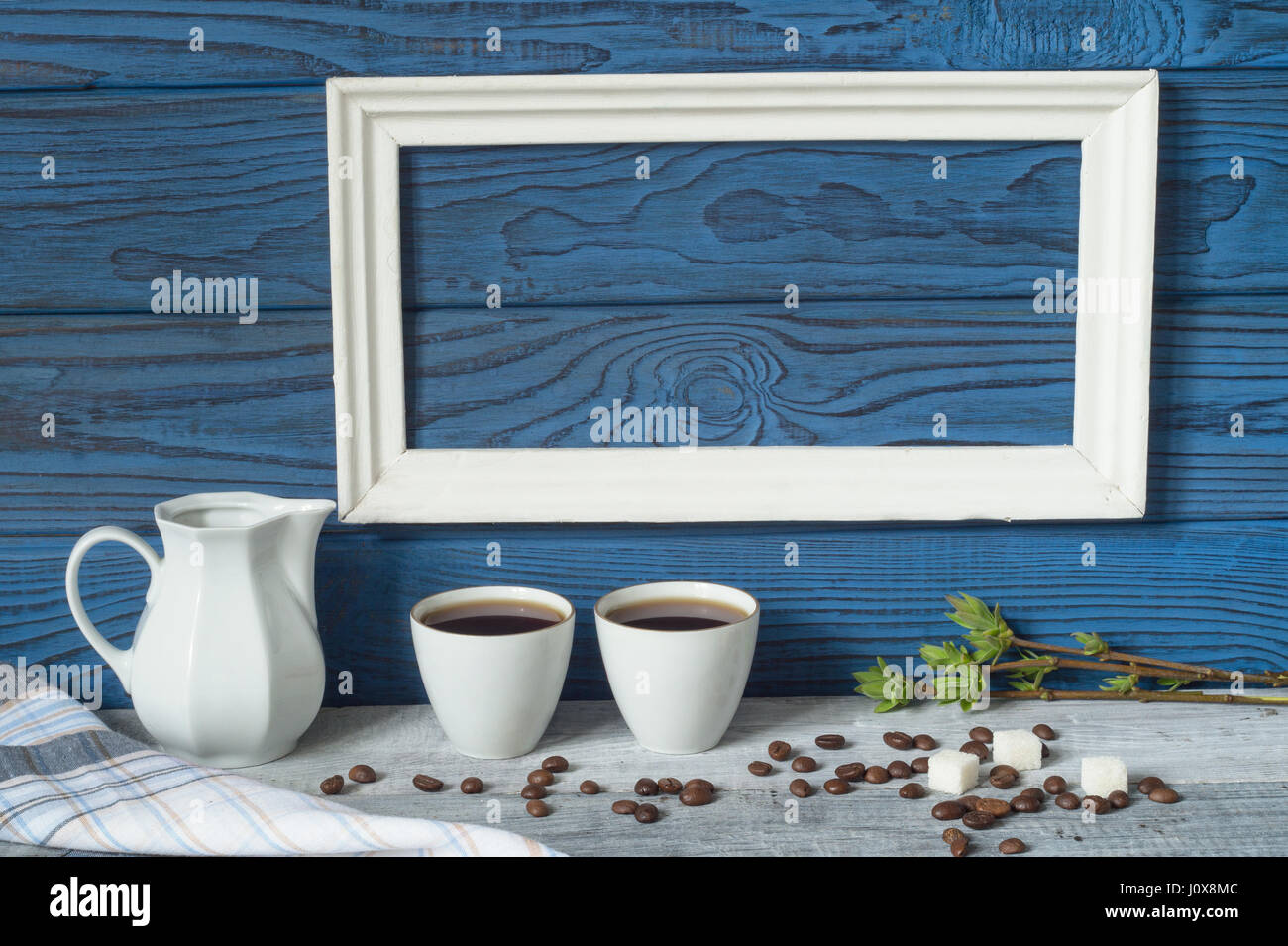 White frame, two coffee cups and a jug on a background of blue boards ...