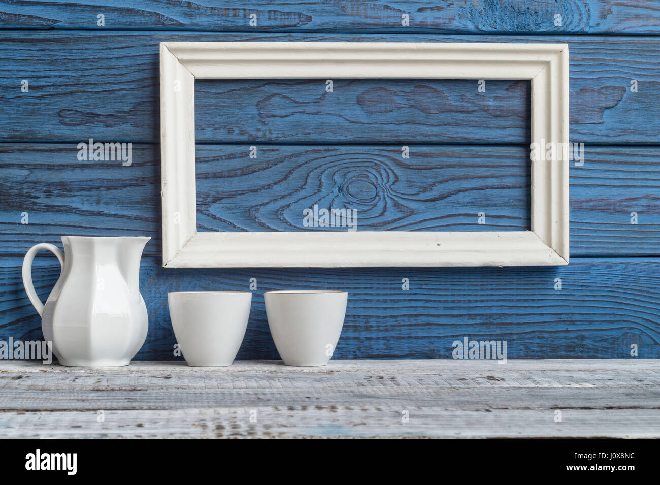 White frame, two coffee cups and a jug on a background of blue boards ...