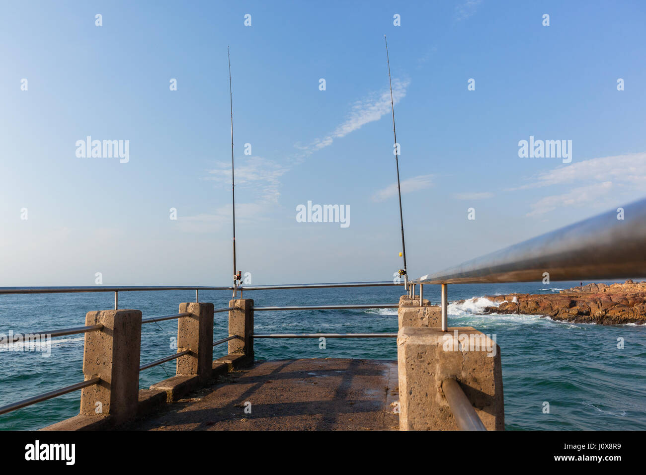 Beach ocean pier jetty with two fishing rods lines out towards blue ...