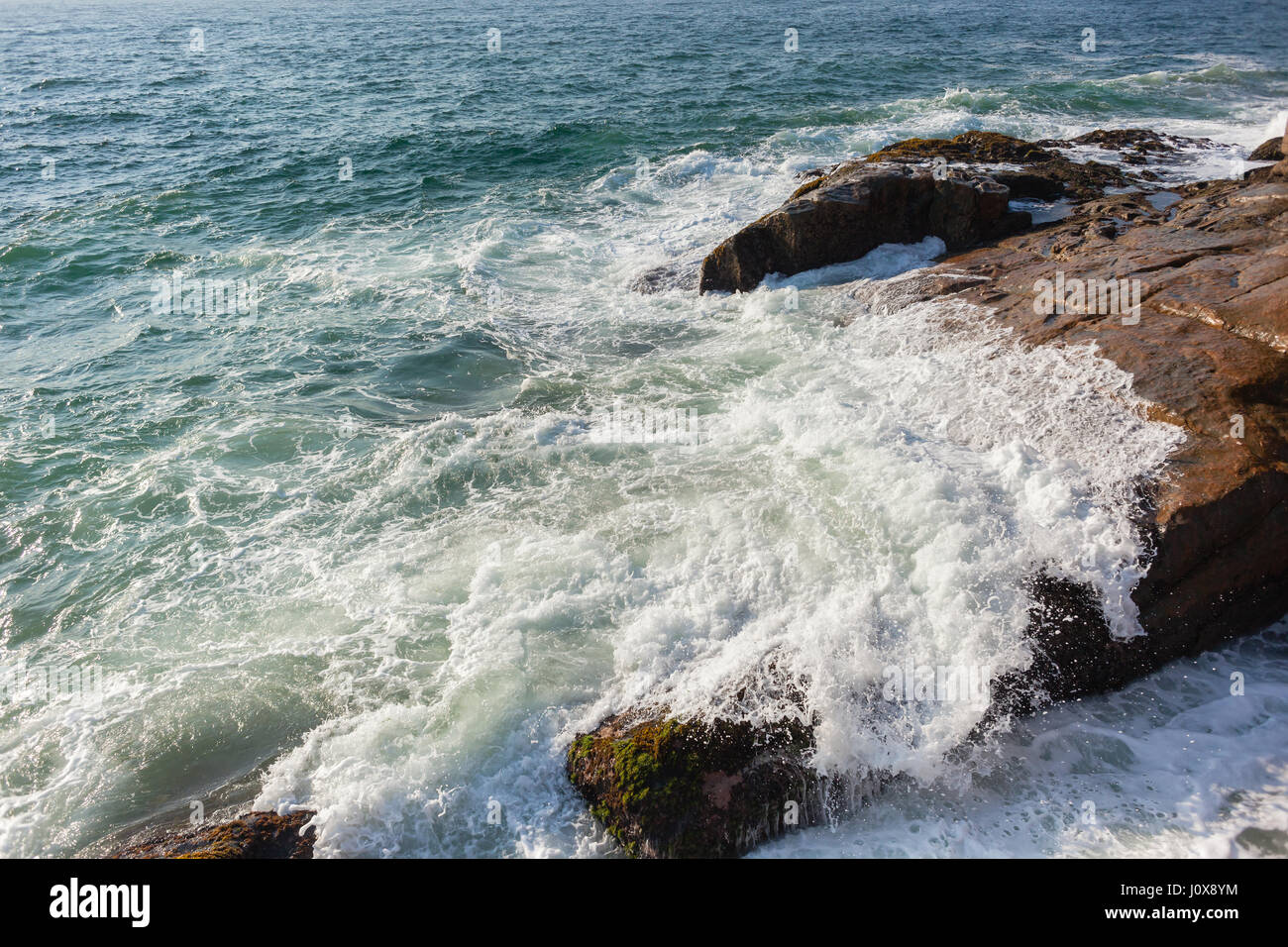 Ocean waves crashing washing over large coastline rocks closeup ...