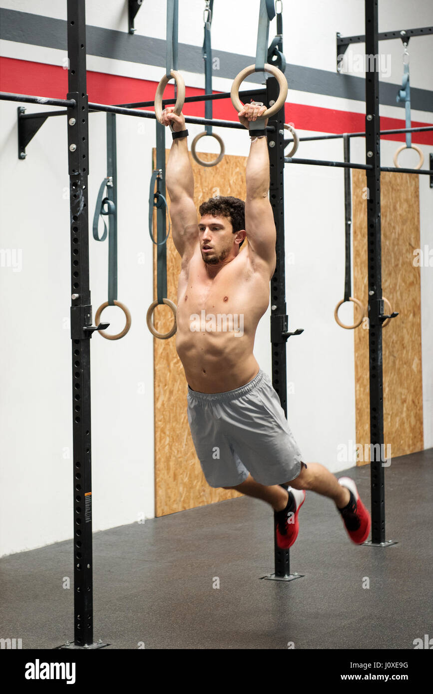 Muscular bare chested young man exercising on rings with toned stomach ...