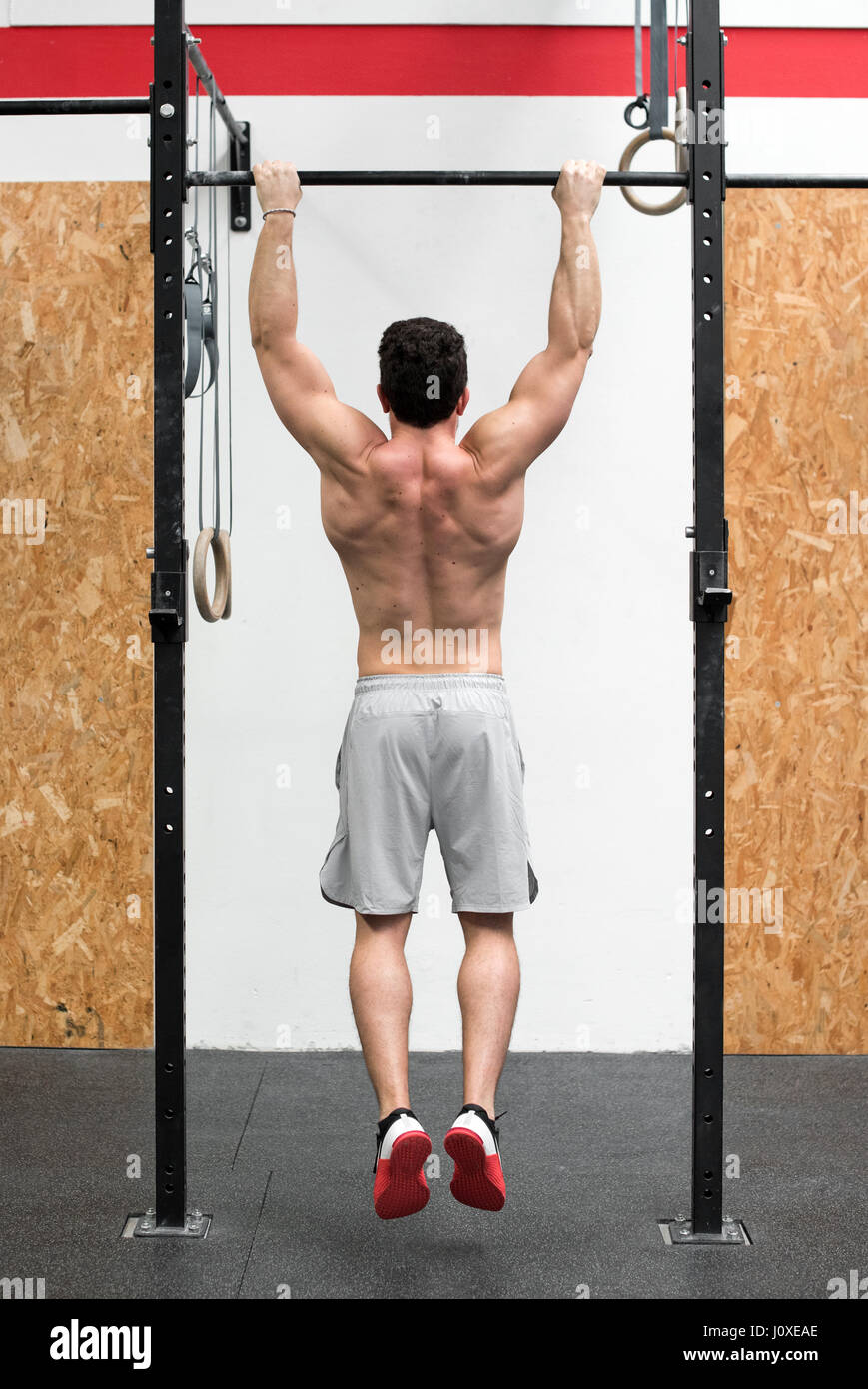 Rear view of muscular bare chested man hanging from rings in gym Stock ...