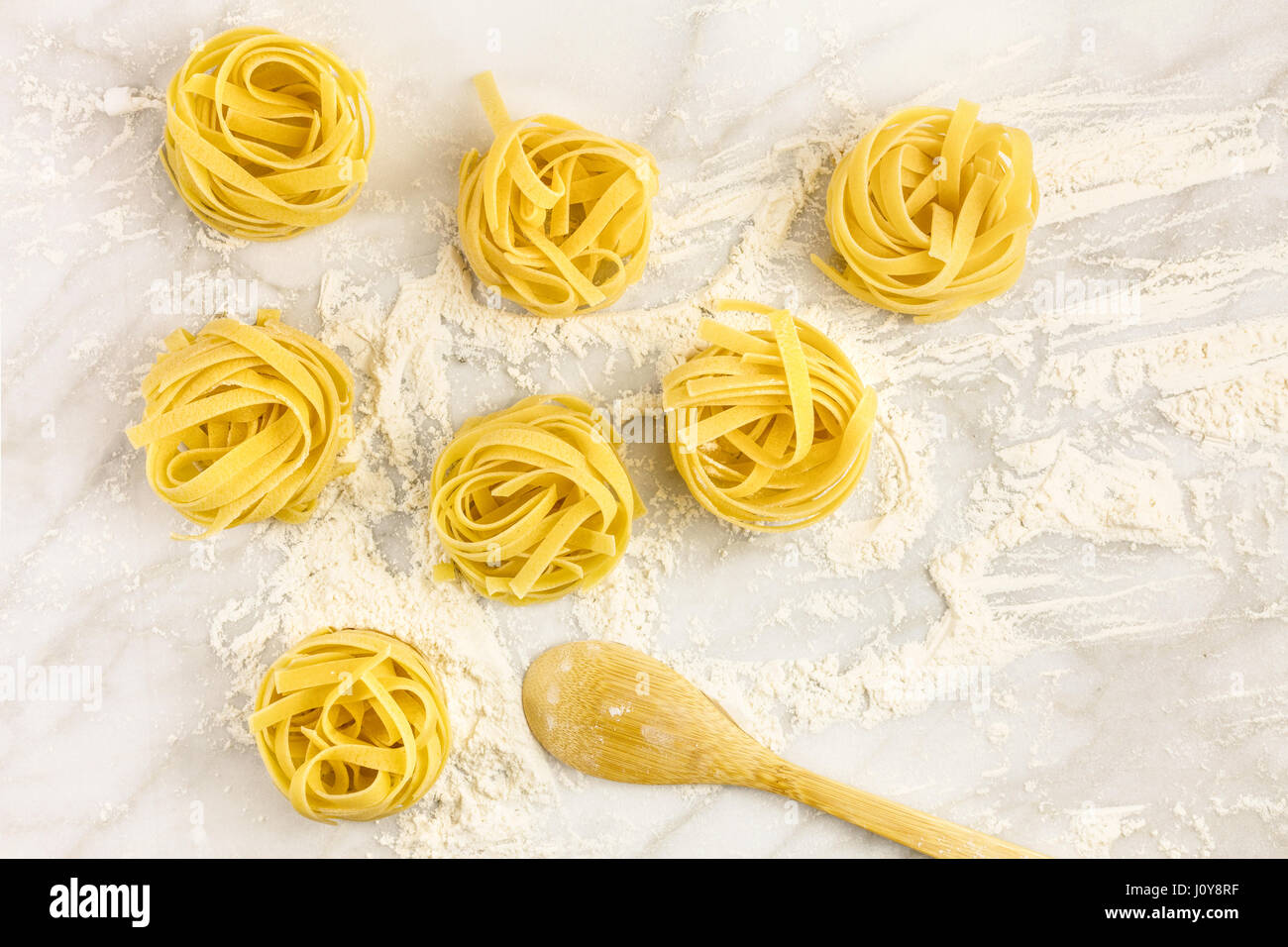 An overhead photo of pasta nests on a white marble table with flour, a ...