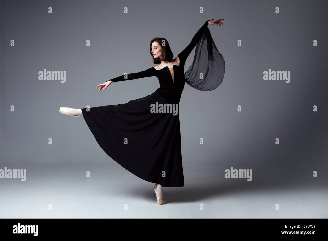 Young slim ballerina in a black long dress is posing and dancing in a ...