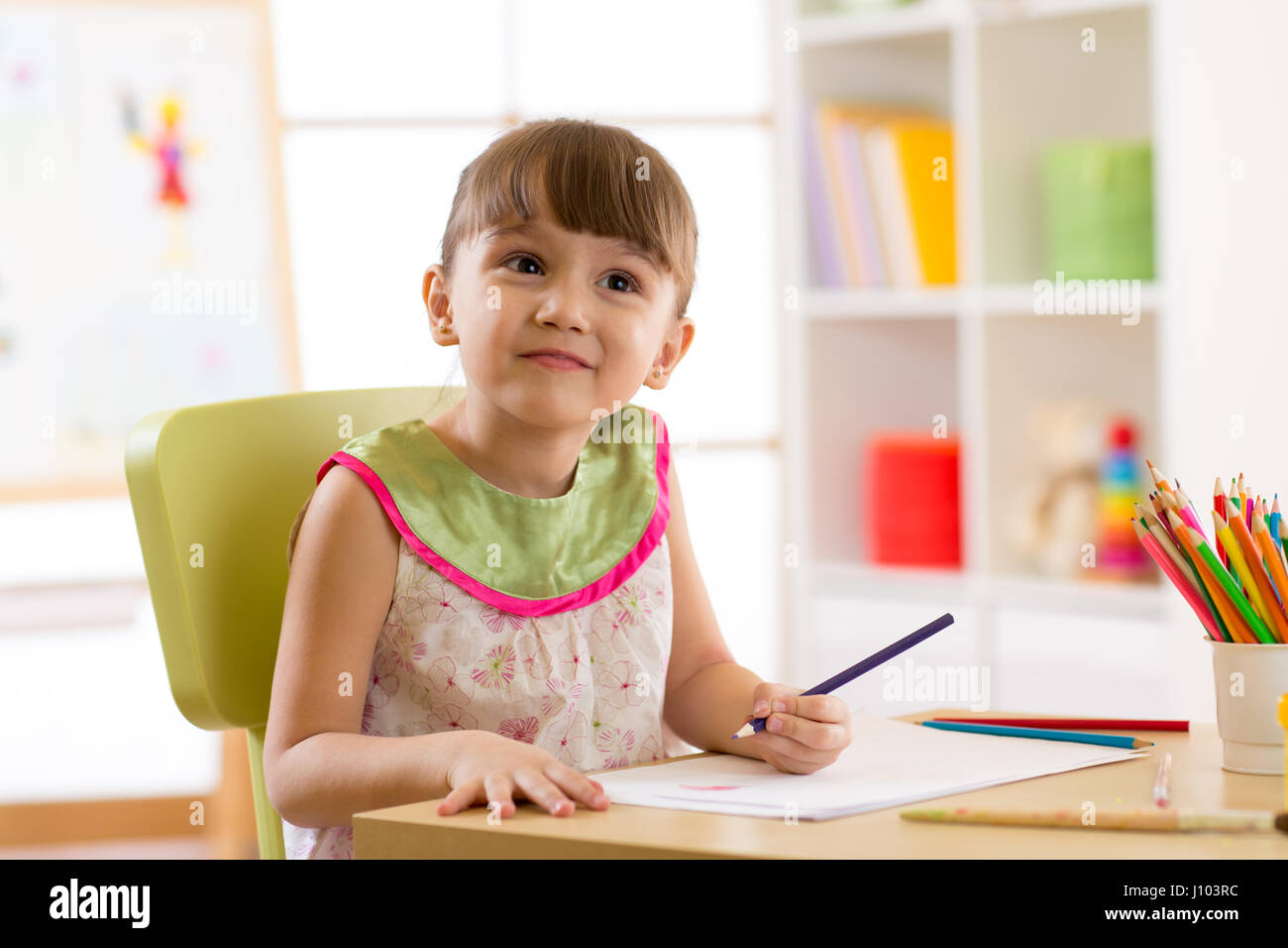 Smiling kid girl drawing with color pencils in day care center Stock ...