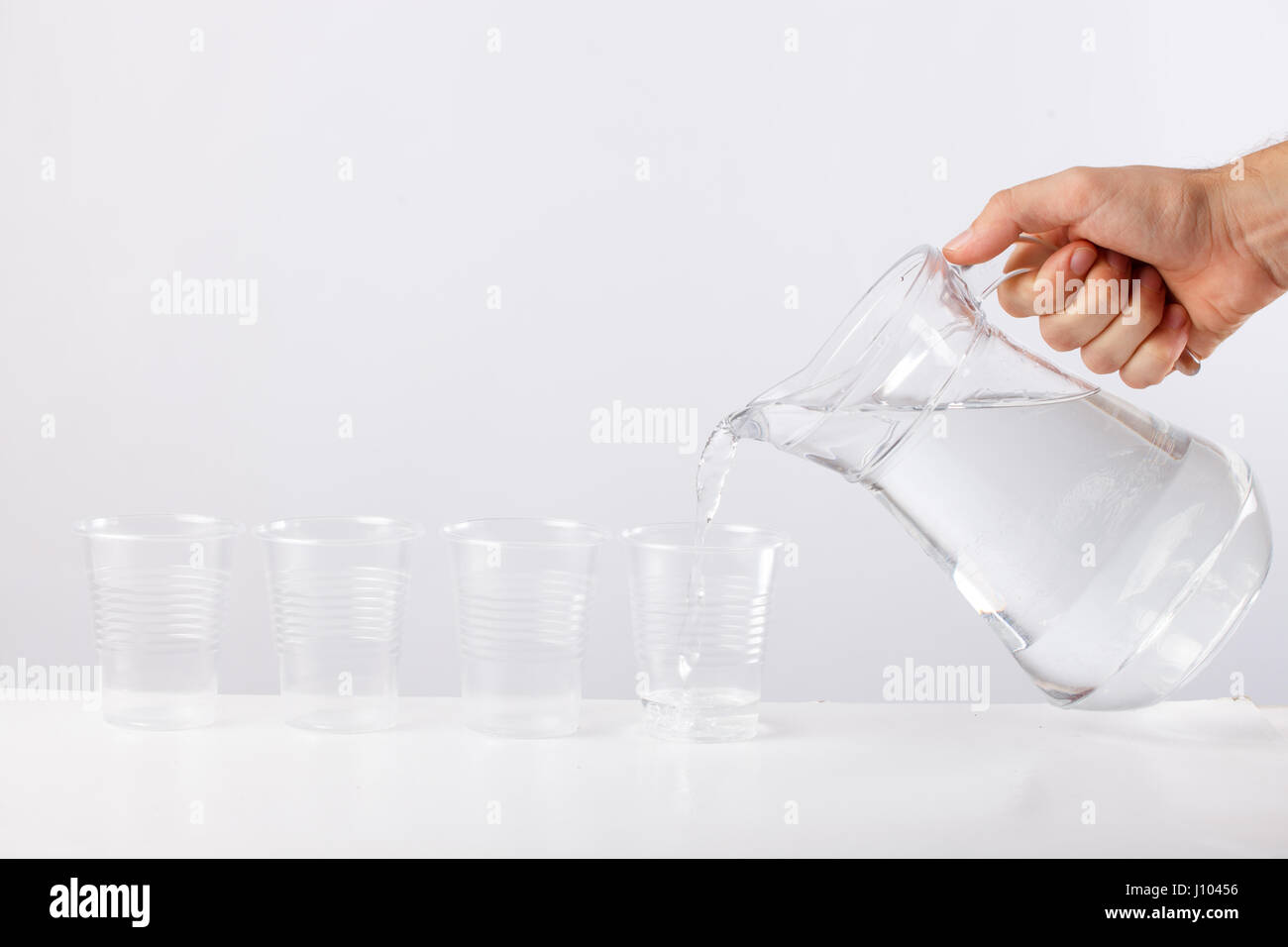 Hand pouring water from glass jug to glass against white background ...
