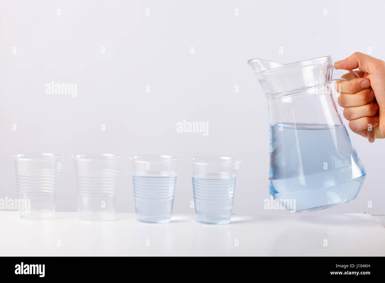 Hand pouring water from glass jug to glass against white background ...