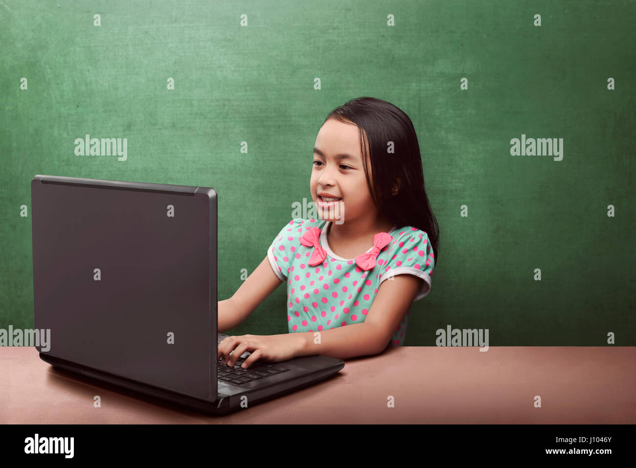 Smiling asian girl using laptop in classroom with chalkboard background ...