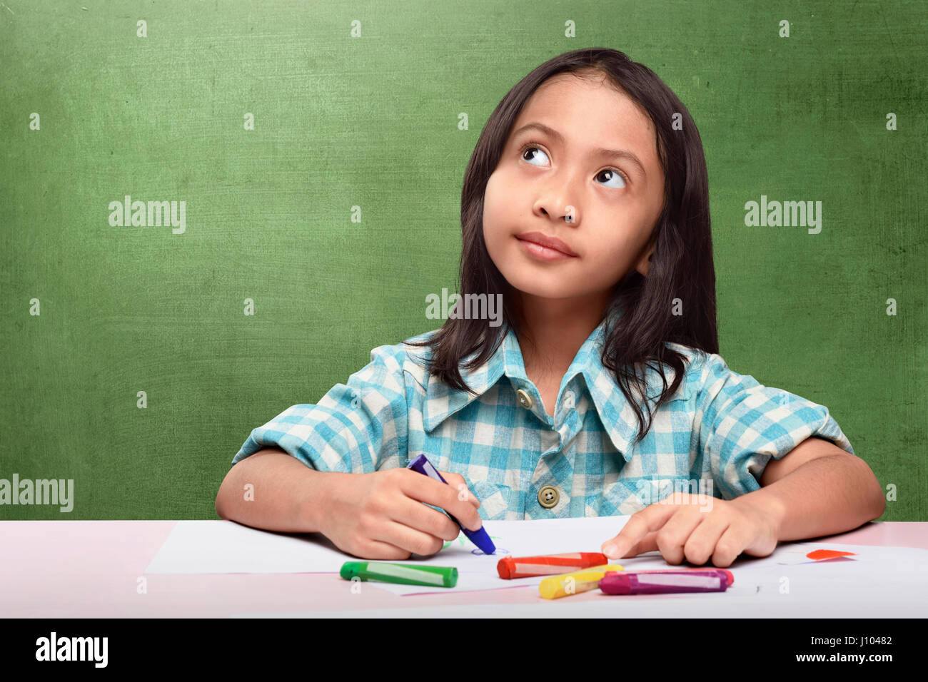 Cheerful asian child imagining something to drawing with crayon at ...