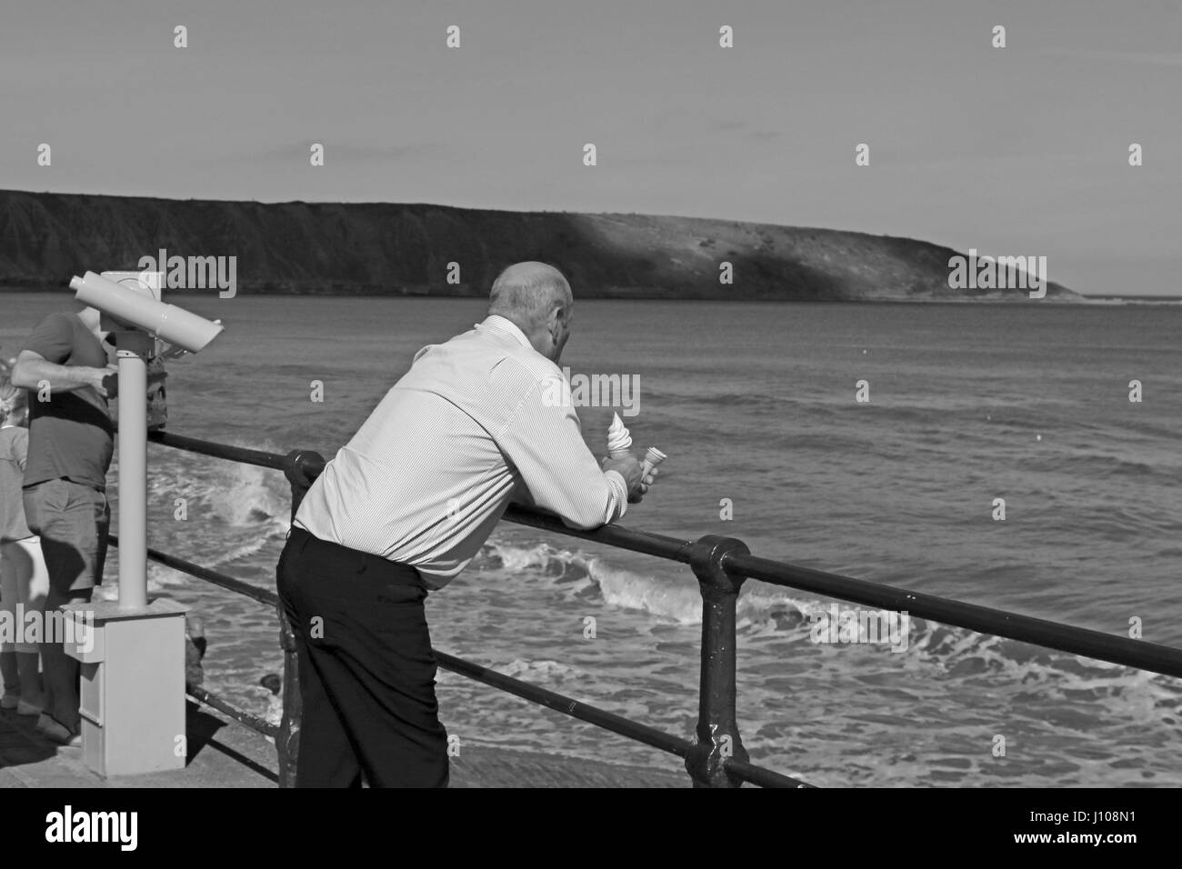 Black and white image of a man with an ice cream watching the sea at ...