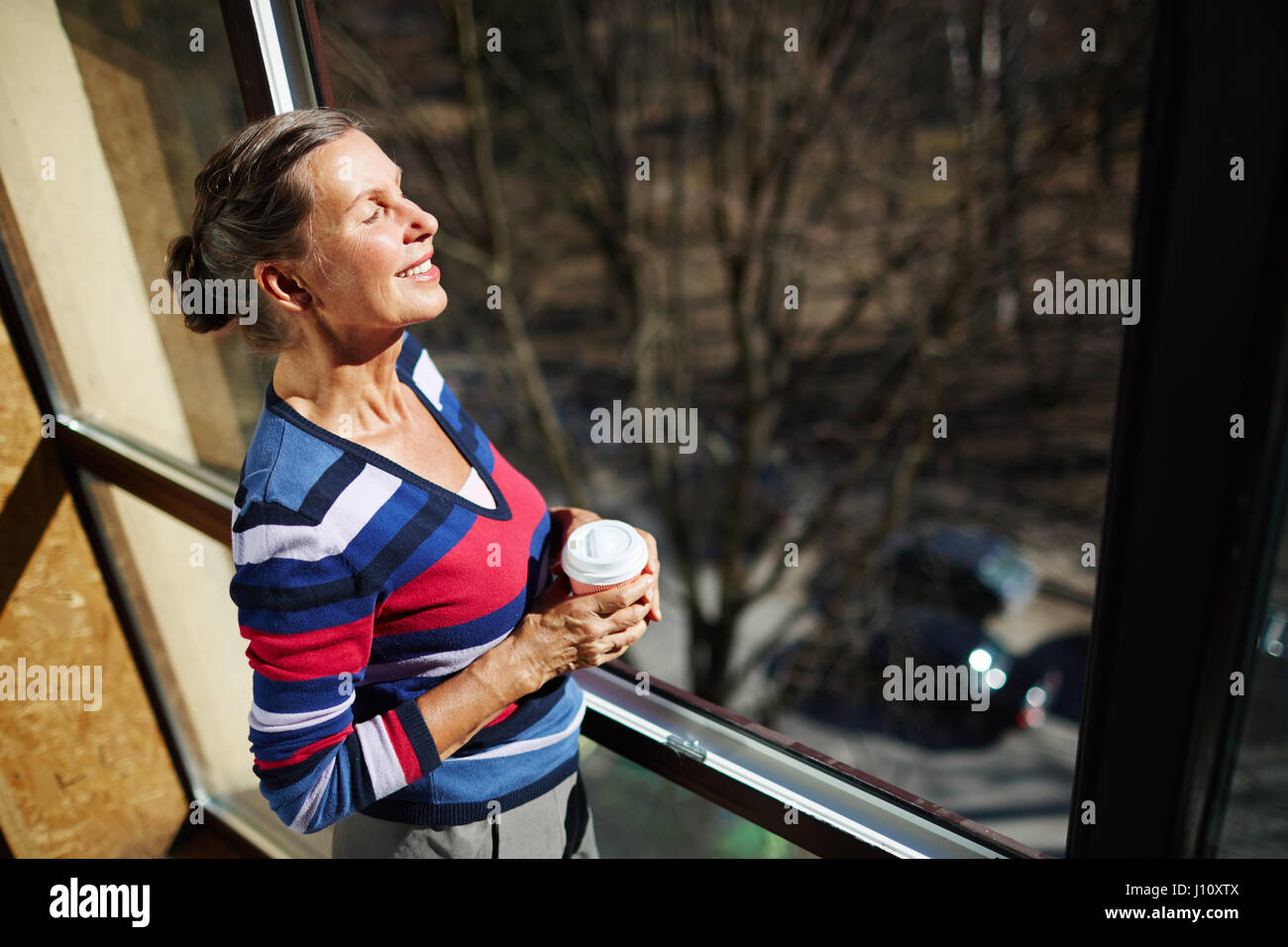 Happy aged woman with drink standing by open window in spring Stock ...