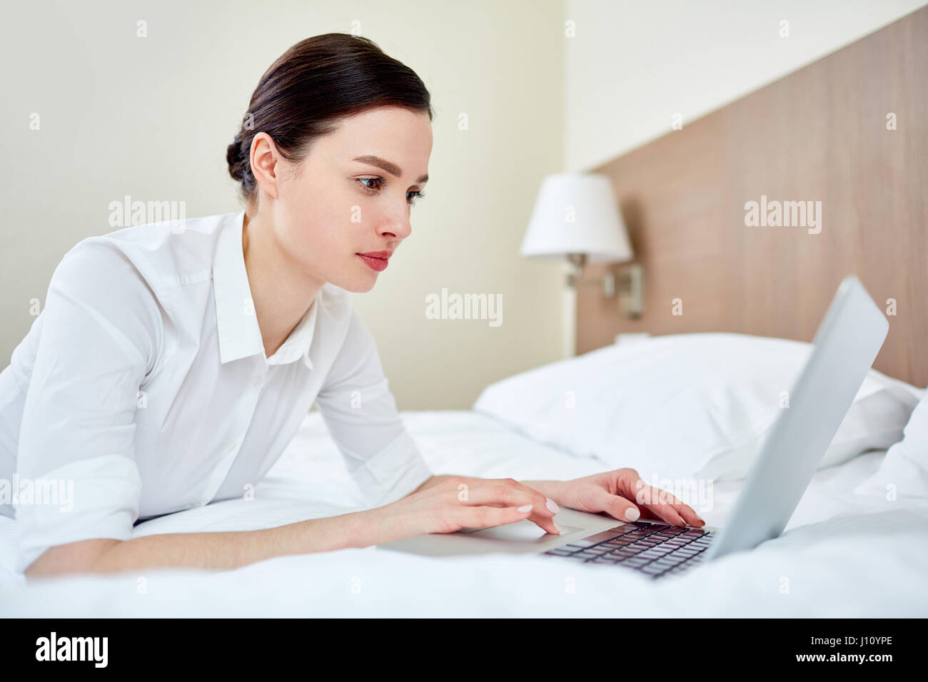 Busy female lying on bed and networking Stock Photo - Alamy
