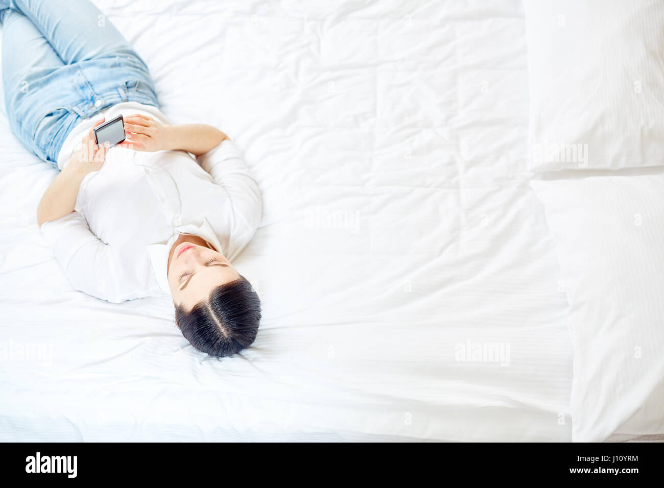 Young woman messaging in smartphone while relaxing on bed Stock Photo ...