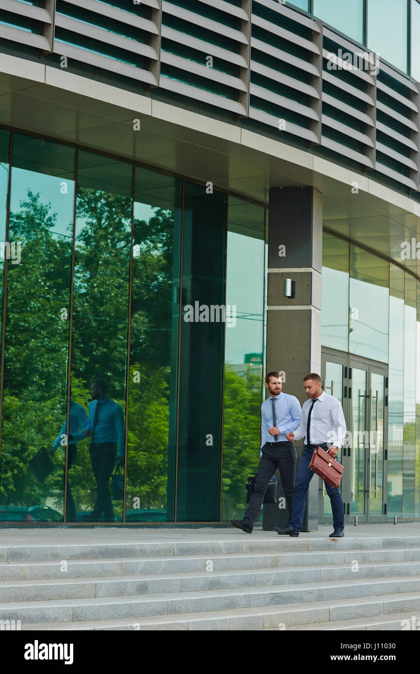 Two young businessmen walking on steps of modern office building with ...