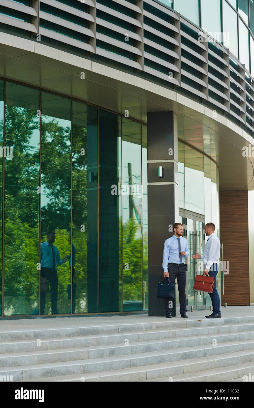 Two young businessmen talking on steps of modern office building with ...