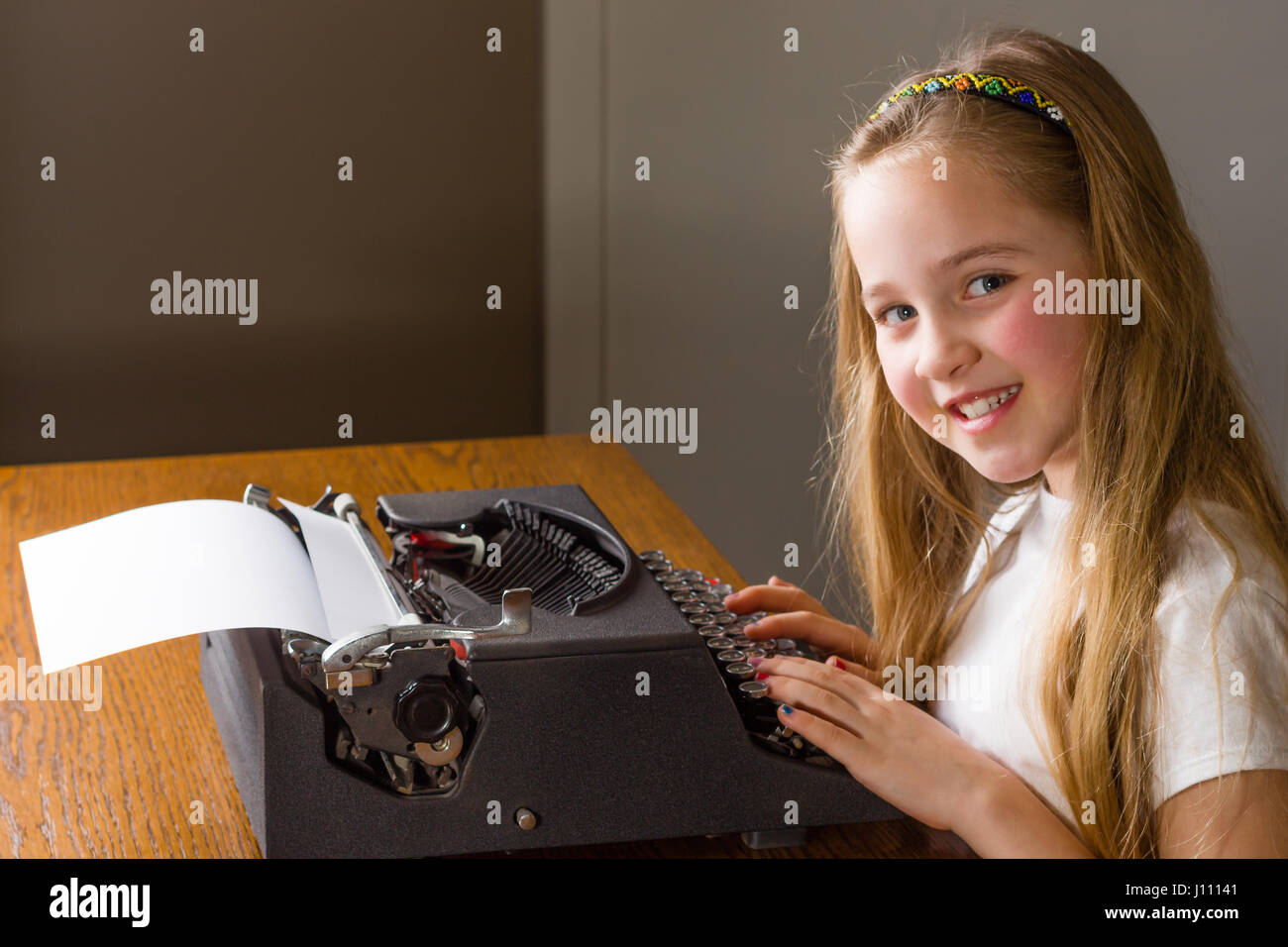 Cute little girl typing a letter on a vintage black typewriter at home ...