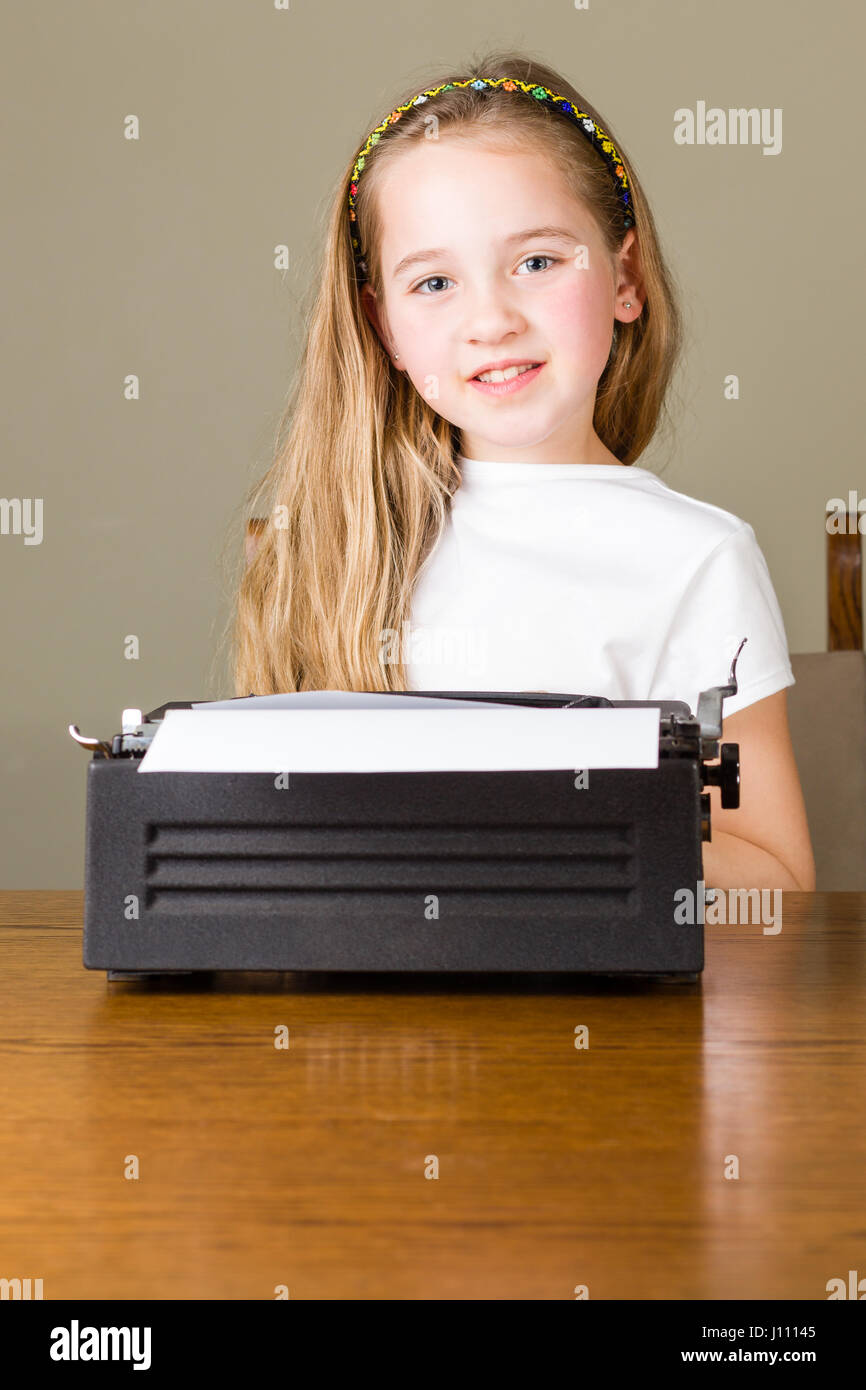 Cute little girl typing a letter on a vintage black typewriter at home ...