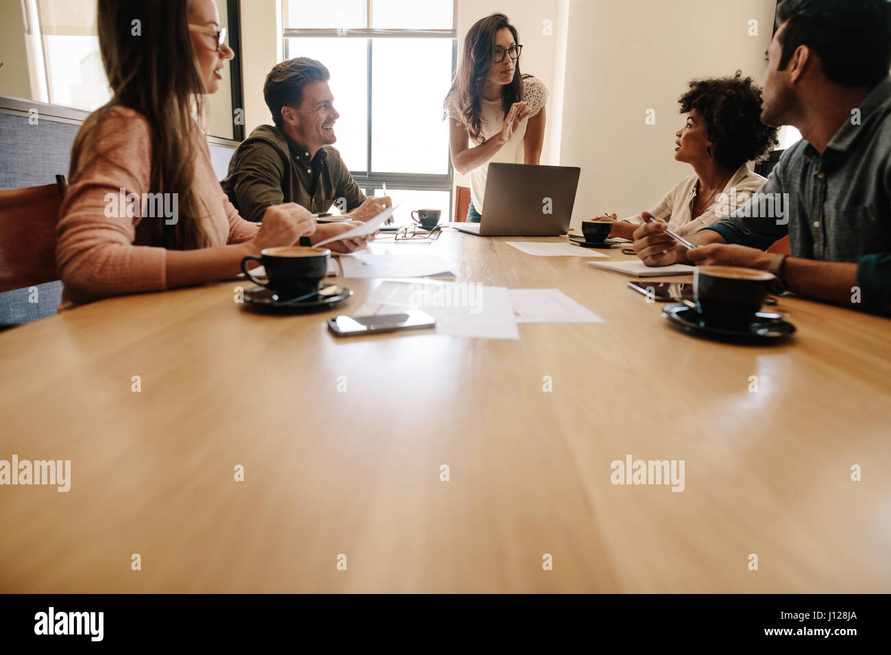 Young woman discussing with group of executives sitting around a table ...