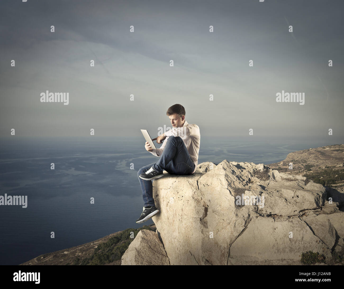 Man with laptop sitting on cliff Stock Photo - Alamy