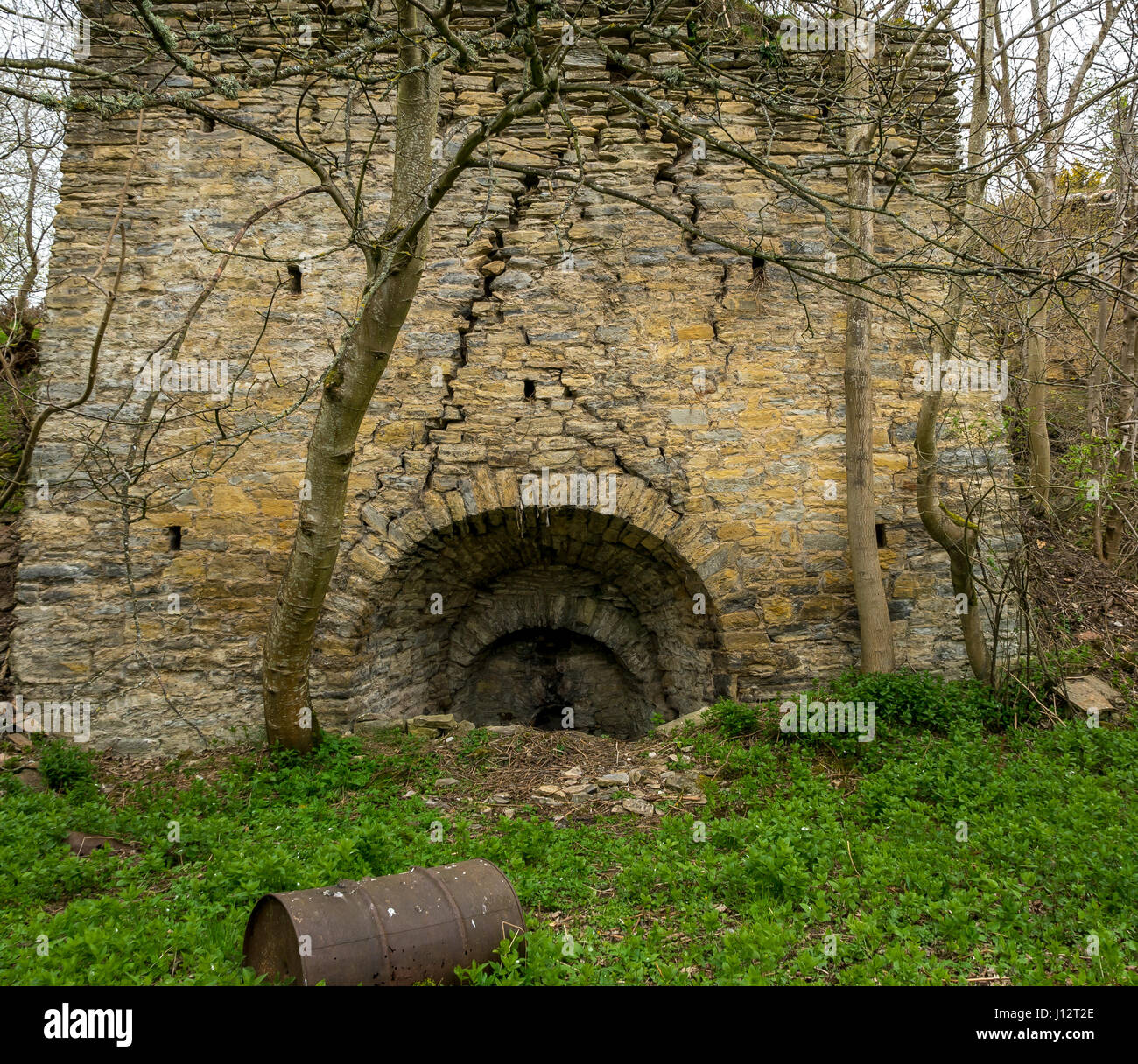 Old overgrown abandoned industrial lime kiln with large rusty oil drum ...