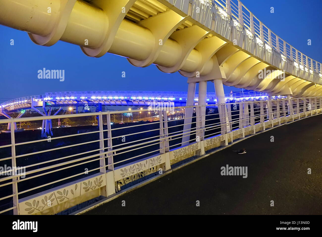 A modern overpass for bikes and pedestrians lit up at evening time ...