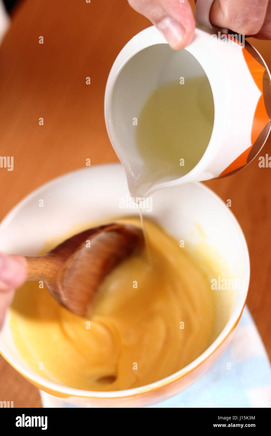 Pouring oil to an egg yolk. Making mayonnaise with a wooden spoon Stock ...