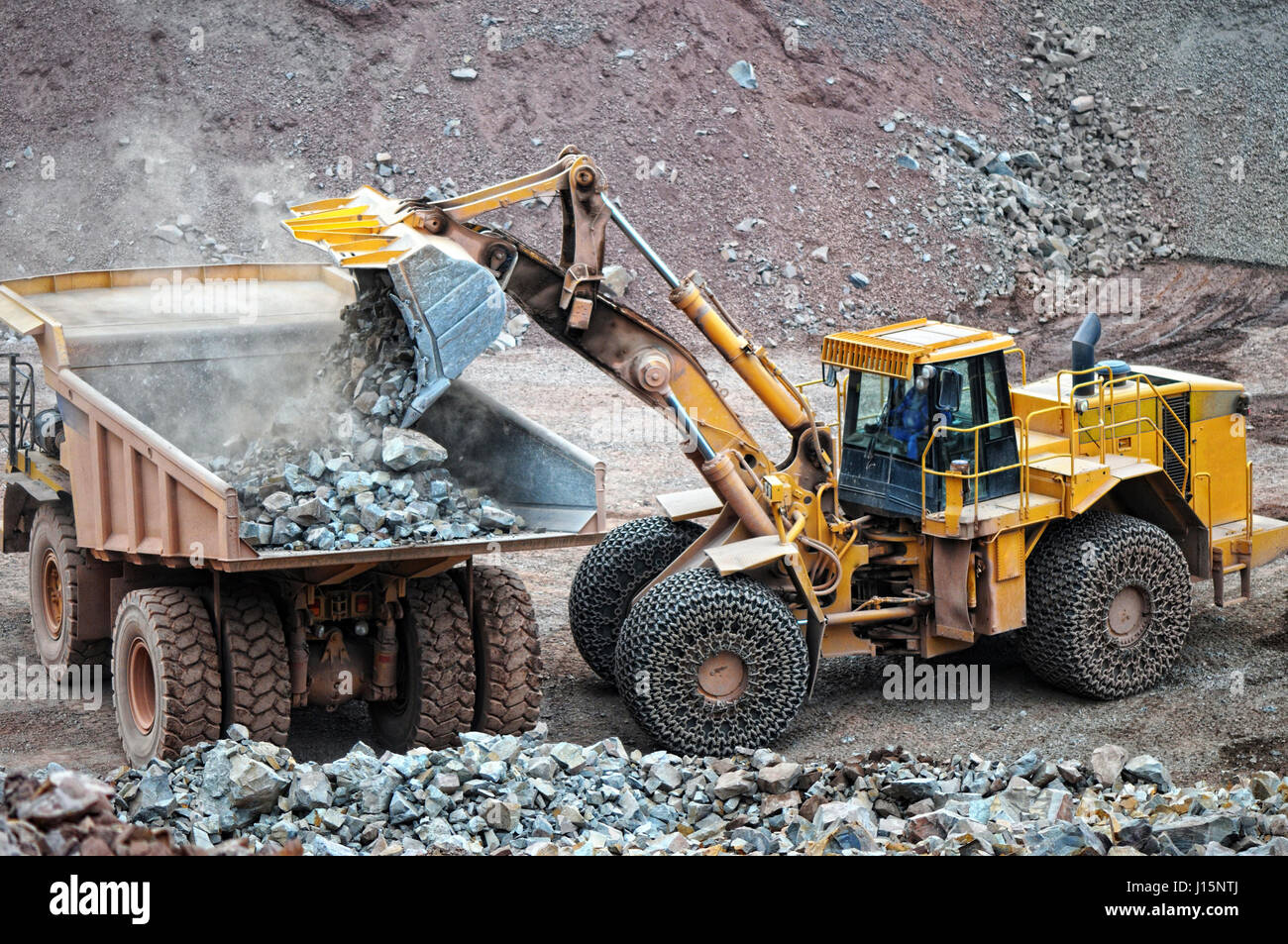 Earthmover loading a dumper truck with rocks. View into a quarry mine ...