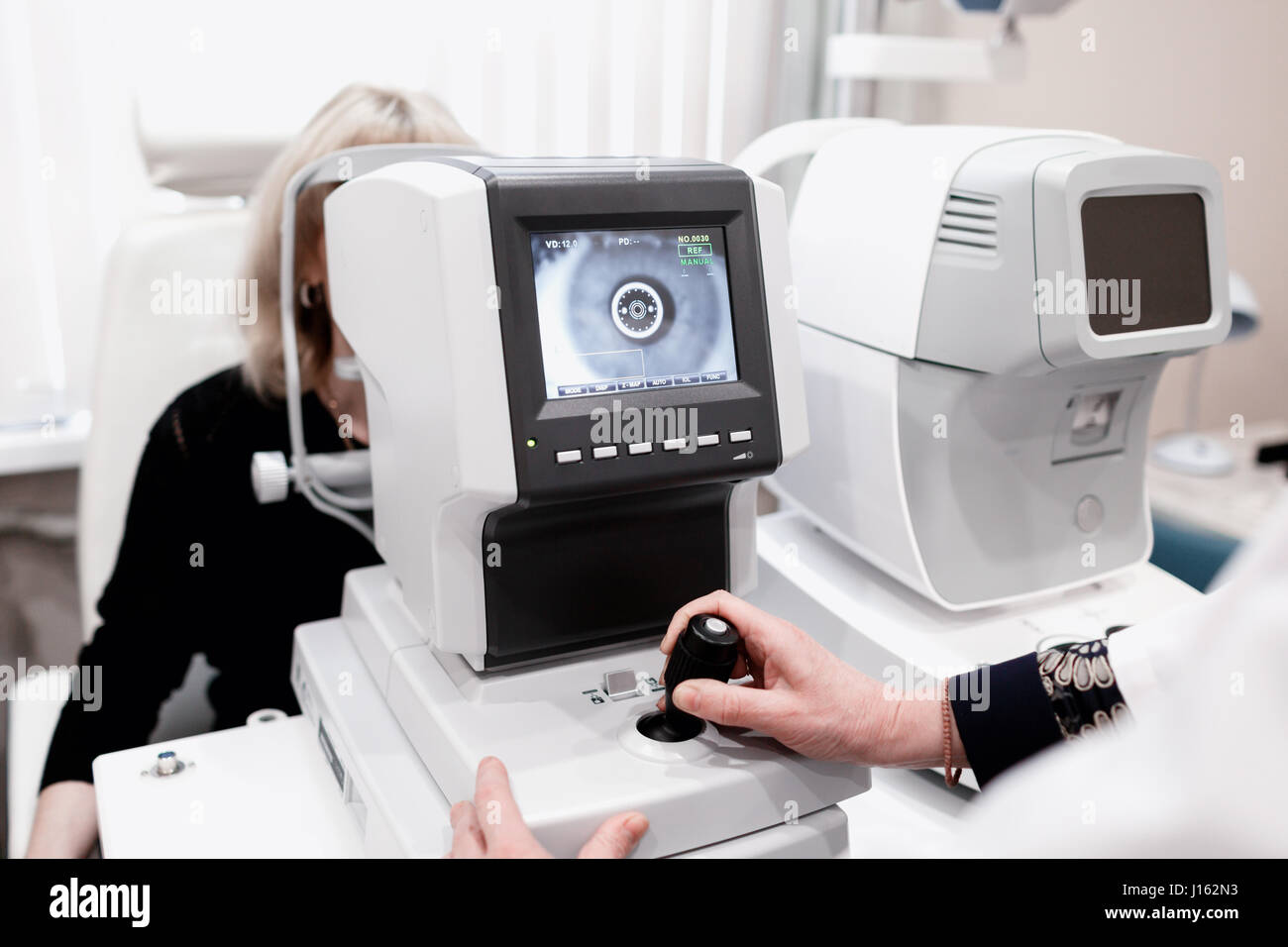Women Looking At Eye Test Machine In Ophthalmology Clinic Stock Photo women-looking-at-eye-test-machine-in-ophthalmology-clinic-stock-photo