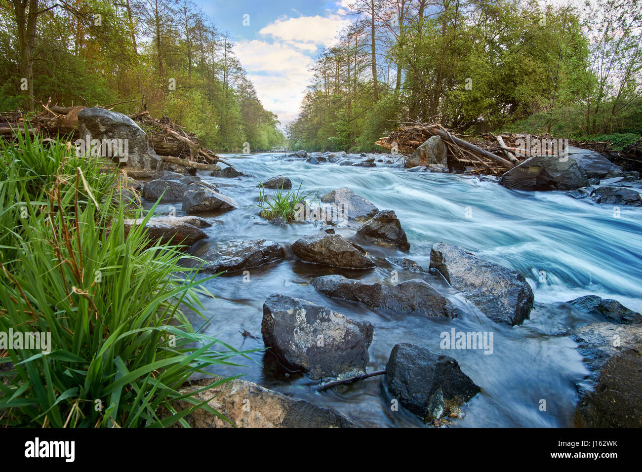 Long exposure from a floating, idyllic river with stones and grass in ...