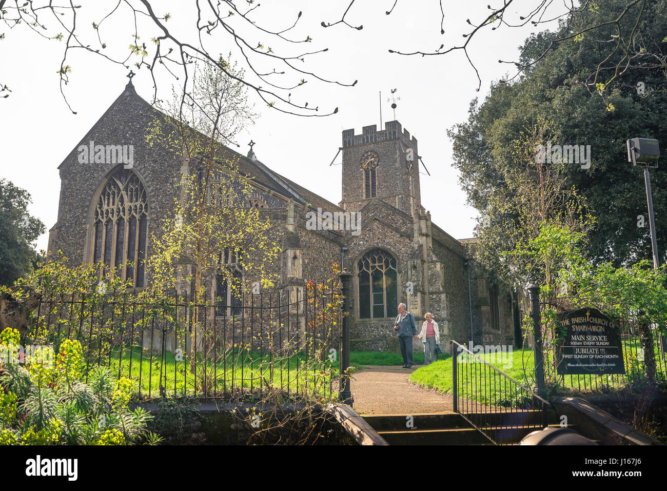 A middle aged couple walk through a churchyard surrounding a medieval ...