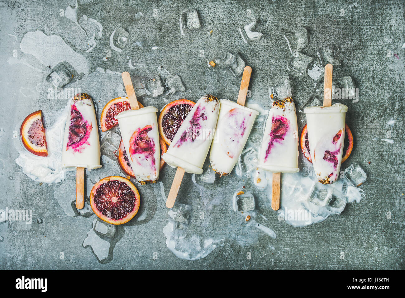 Red orange, yogurt, granola popsicles on ice cubes, grey background ...