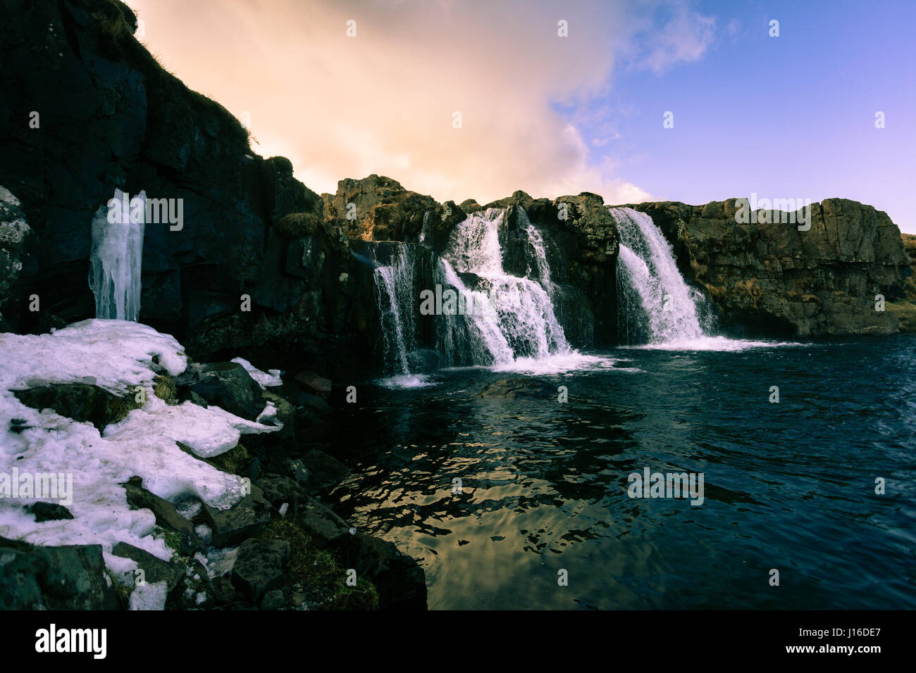 Sunset over a waterfall near Kirkjufell mountain in the Snæfellsnes ...