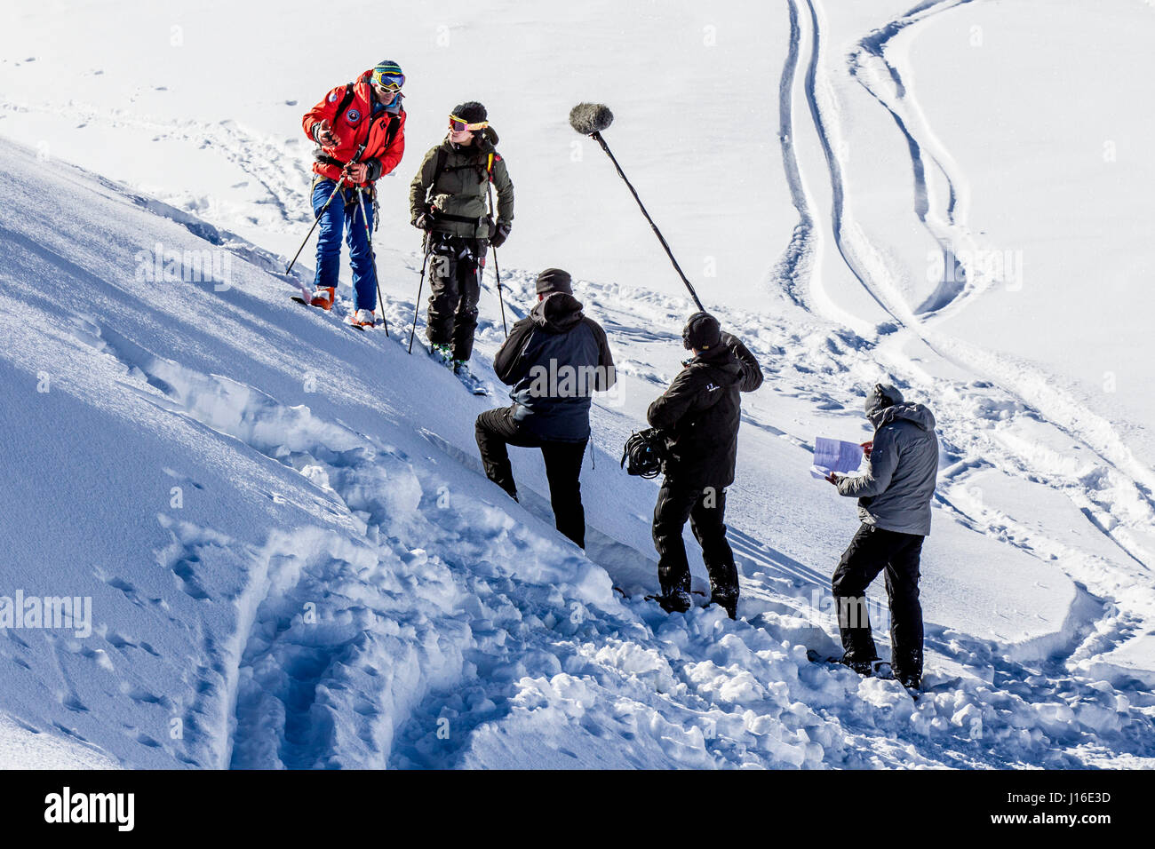 Crew standing in snow filming mountain guide discussing avalanche ...