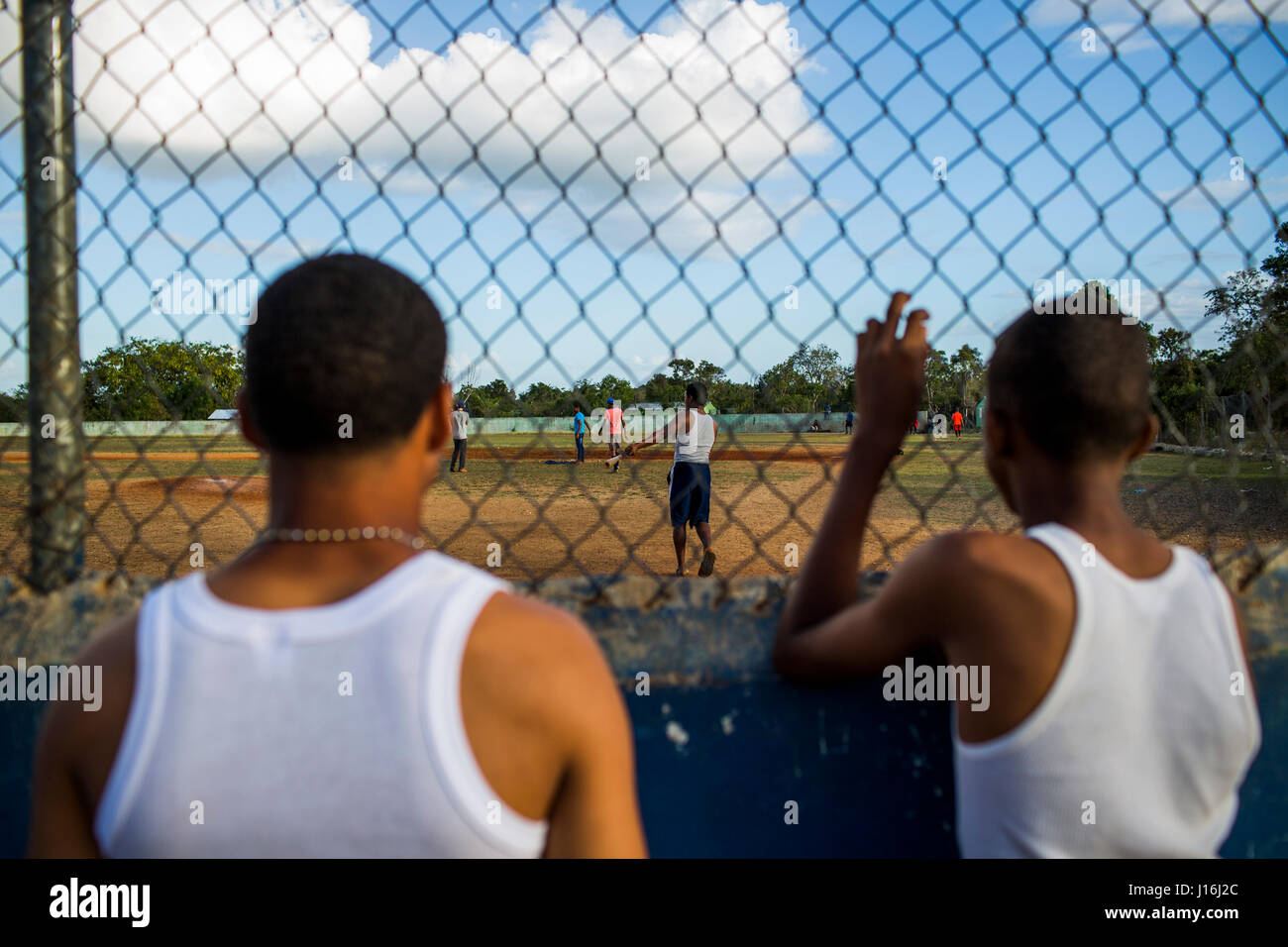 Two Young Men In White Tank Tops Watch A Sandlot Baseball Game Through ...