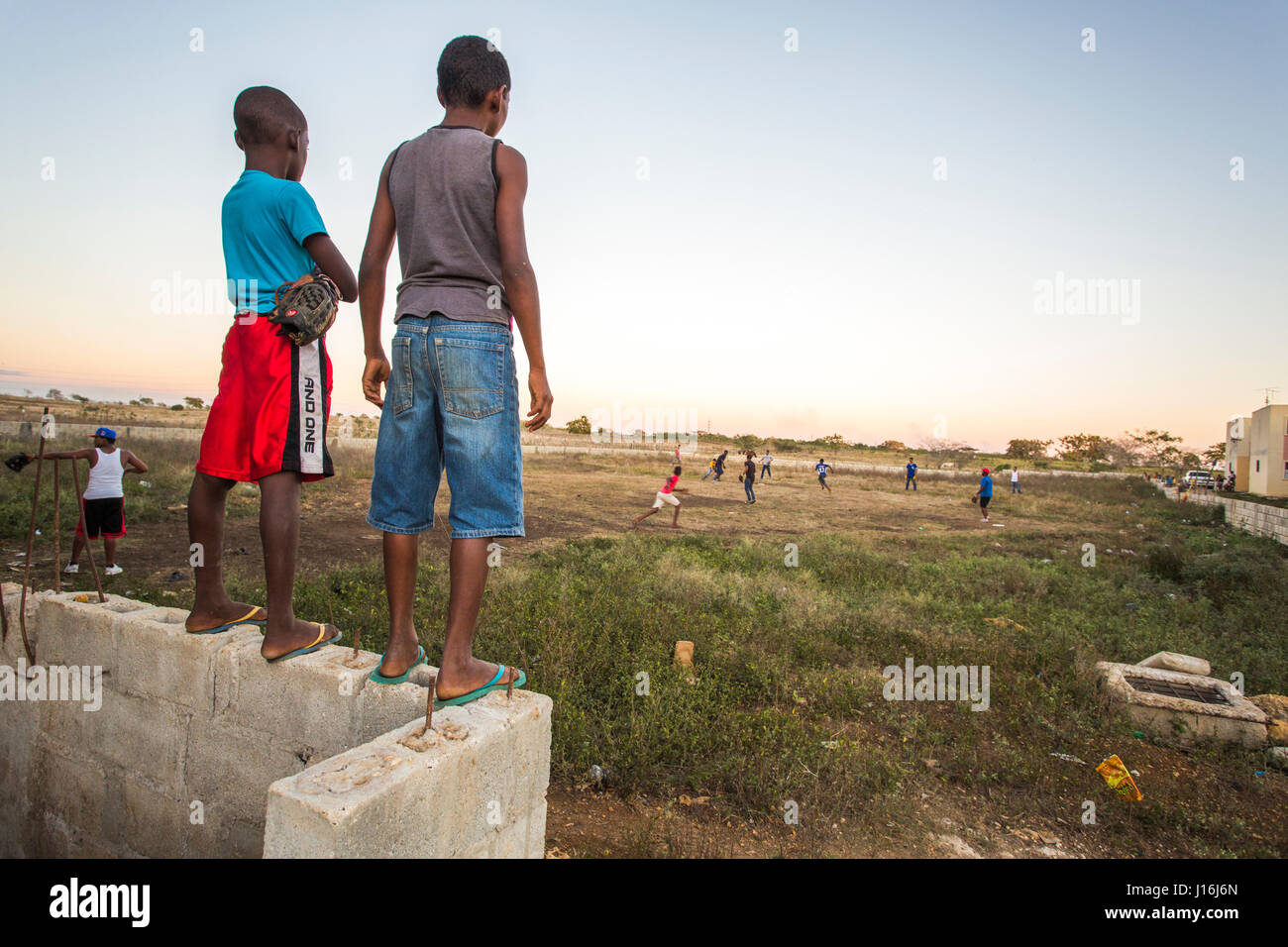 Two Boys Stand On A Wall Overlooking A Pick-up Baseball Game On A Rural ...