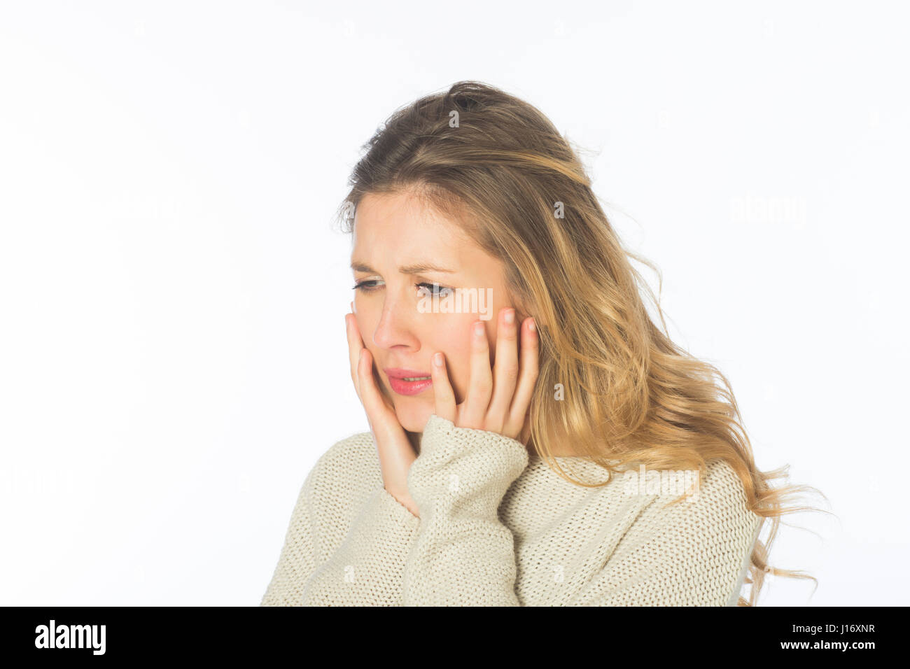 Stressed young blond woman hands on face looking away against a white ...