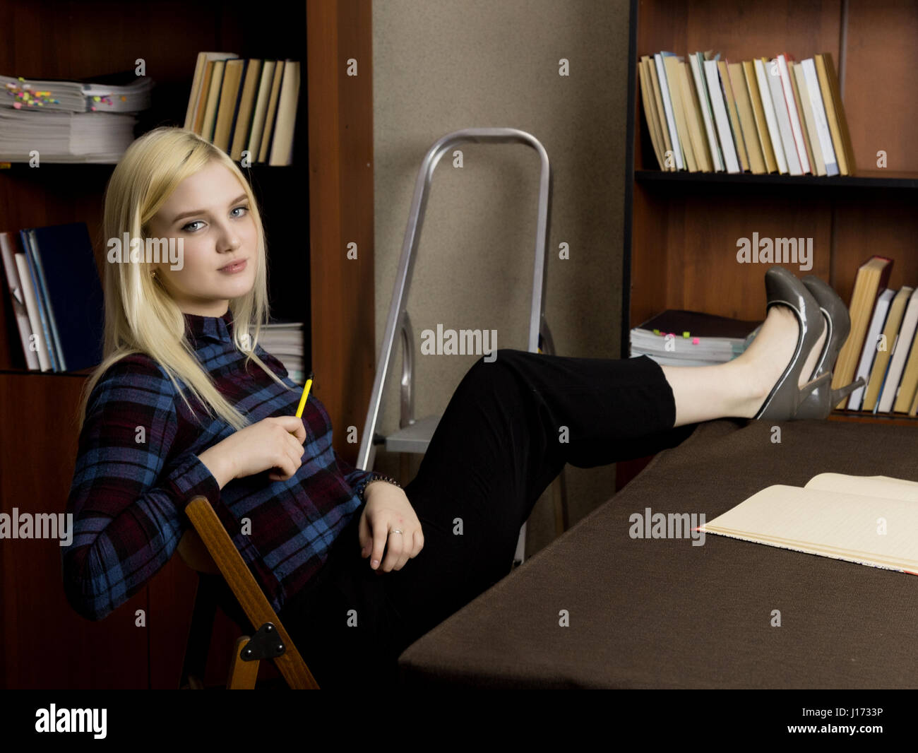 young female librarian reading a big book in library. bookshelves with ...