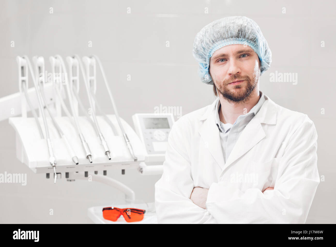 Portrait of happy male dentist wearing lab coat while sitting in clinic ...